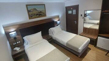 Quarto de hotel com duas camas de solteiro, uma escrivaninha com luminária, um pequeno frigorífico e um espelho.