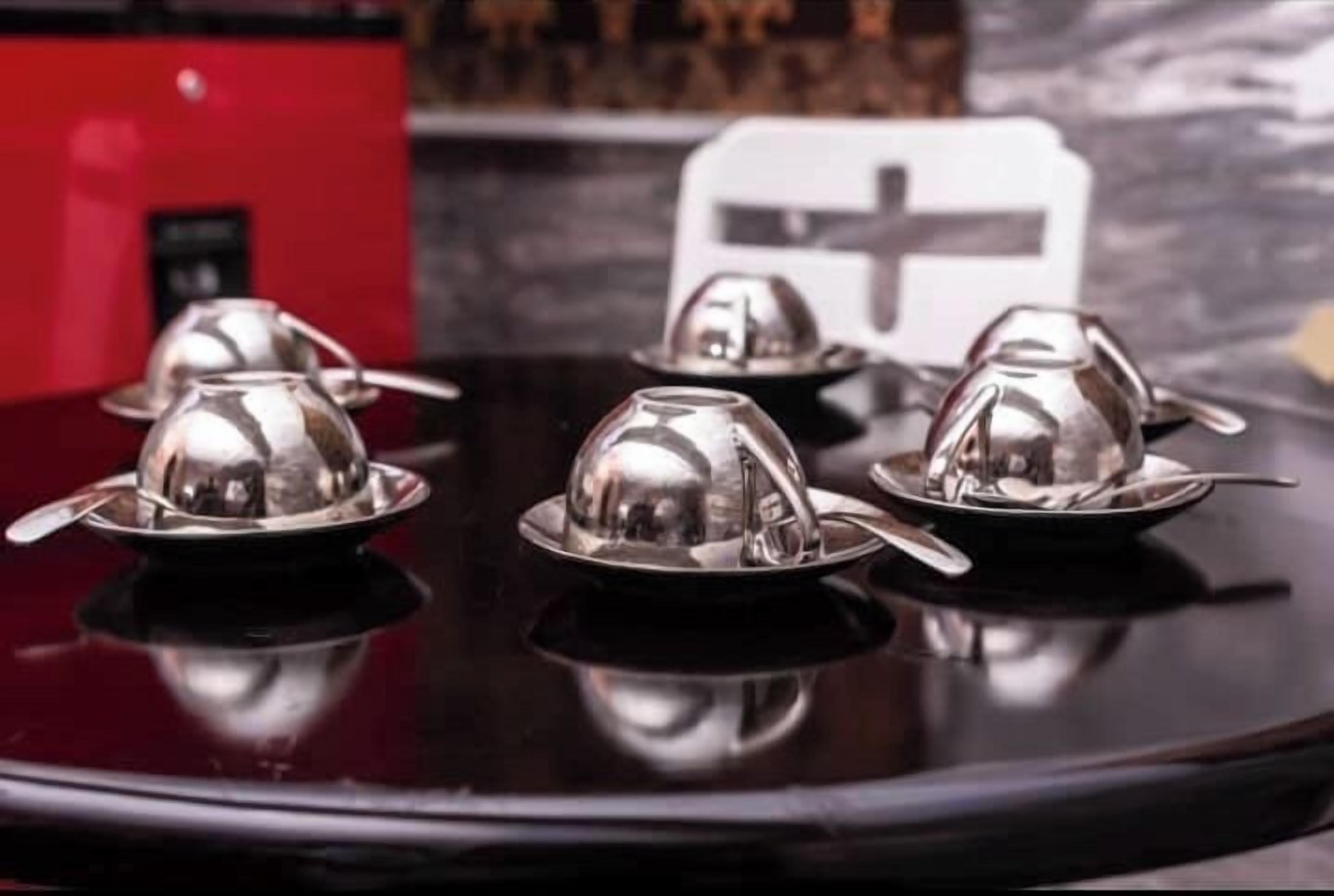 Uma mesa com quatro pires e colheres de metal, refletindo em uma superfície escura.