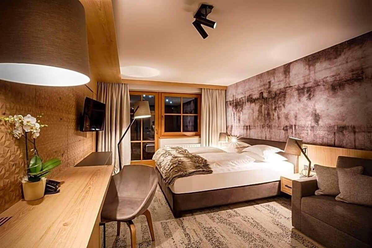 Quarto de hotel moderno com uma cama grande, uma escrivaninha, uma cadeira e uma televisão.
