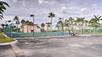 Uma quadra esportiva com grade, palmeiras e um edifício com torre do relógio.