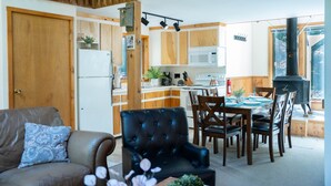 Cozinha moderna com armários de madeira, área de jantar com mesa e cadeiras, e sala de estar aconchegante com sofá e almofada decorativa.