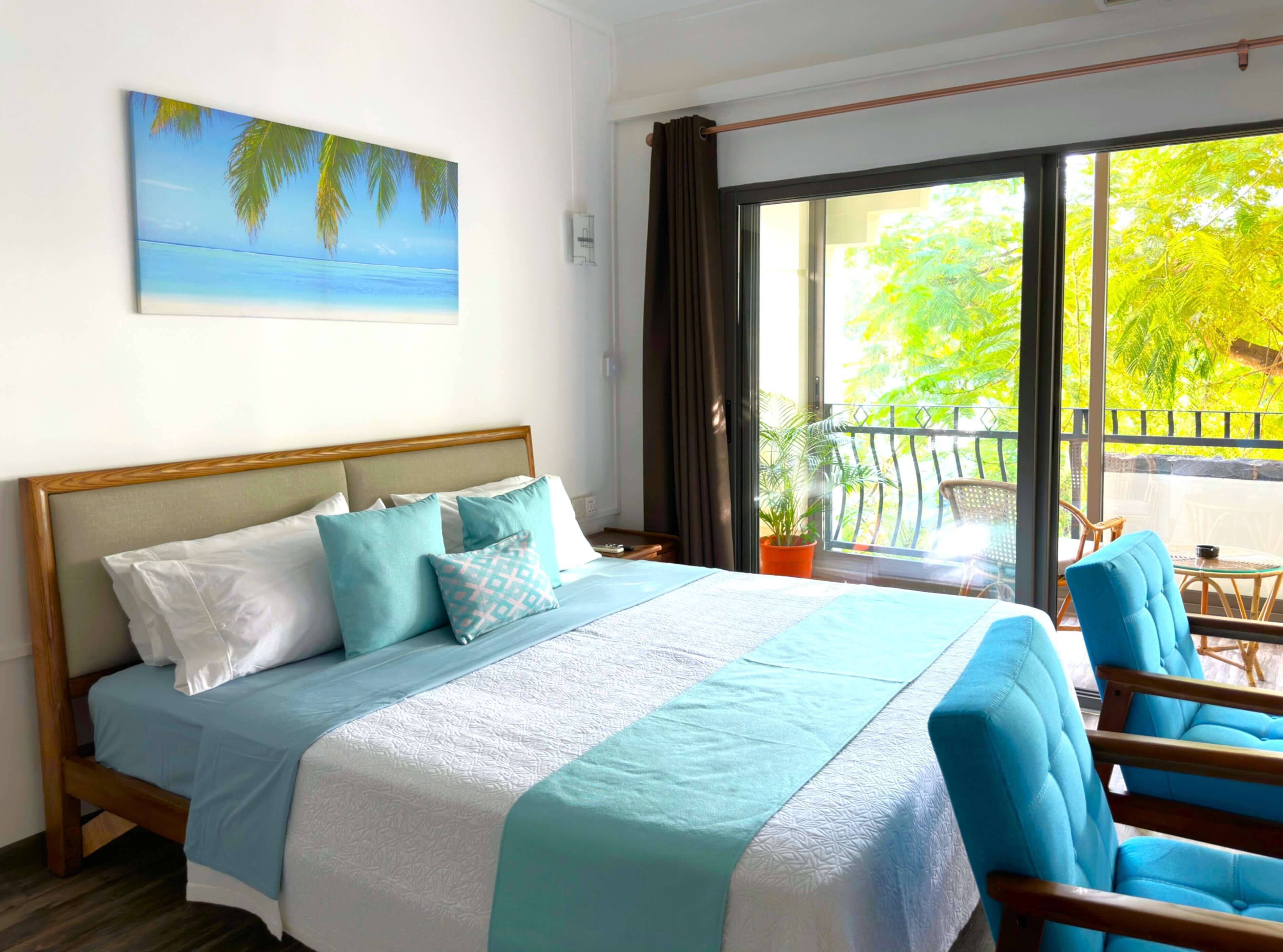 Quarto de hotel com cama, vista para o exterior e varanda com cadeiras.