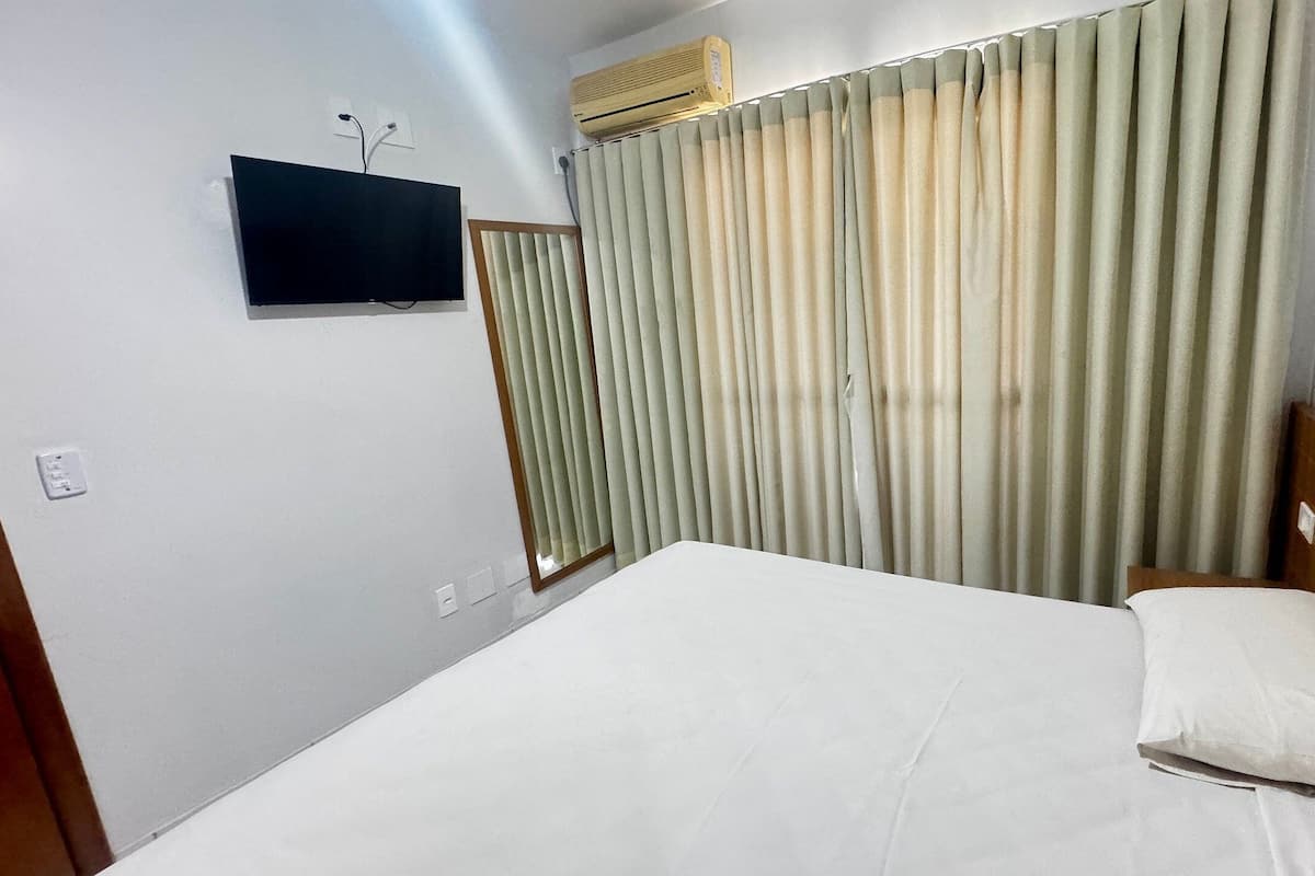 Quarto de hotel com uma cama, televisão na parede e janela com cortinas.