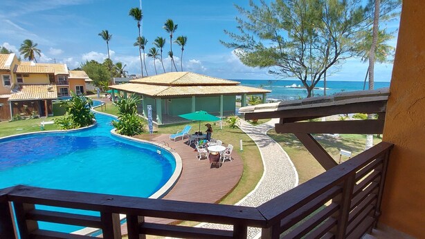 Área de piscina com piscina em formato curvo, cadeiras de descanso e um pequeno pavilhão.