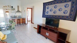 Uma sala de estar com sofá, rack para TV e área de jantar com cadeiras e mesa.