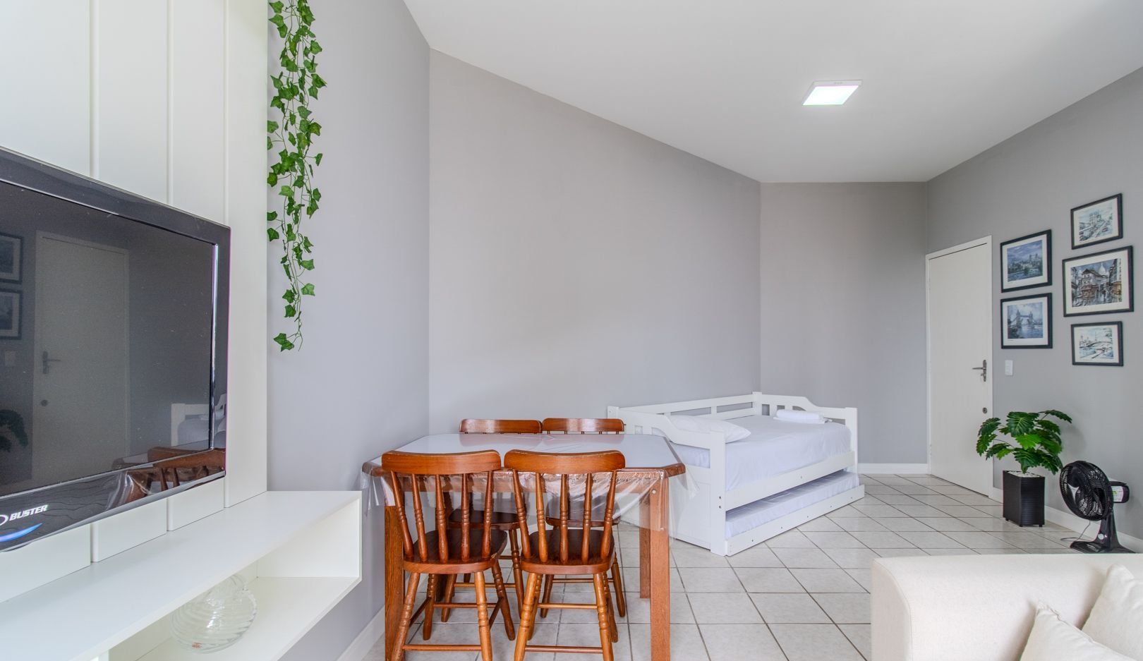 Uma sala de estar moderna com um sofá branco, uma mesa de jantar com cadeiras, uma cama branca e uma televisão na parede.