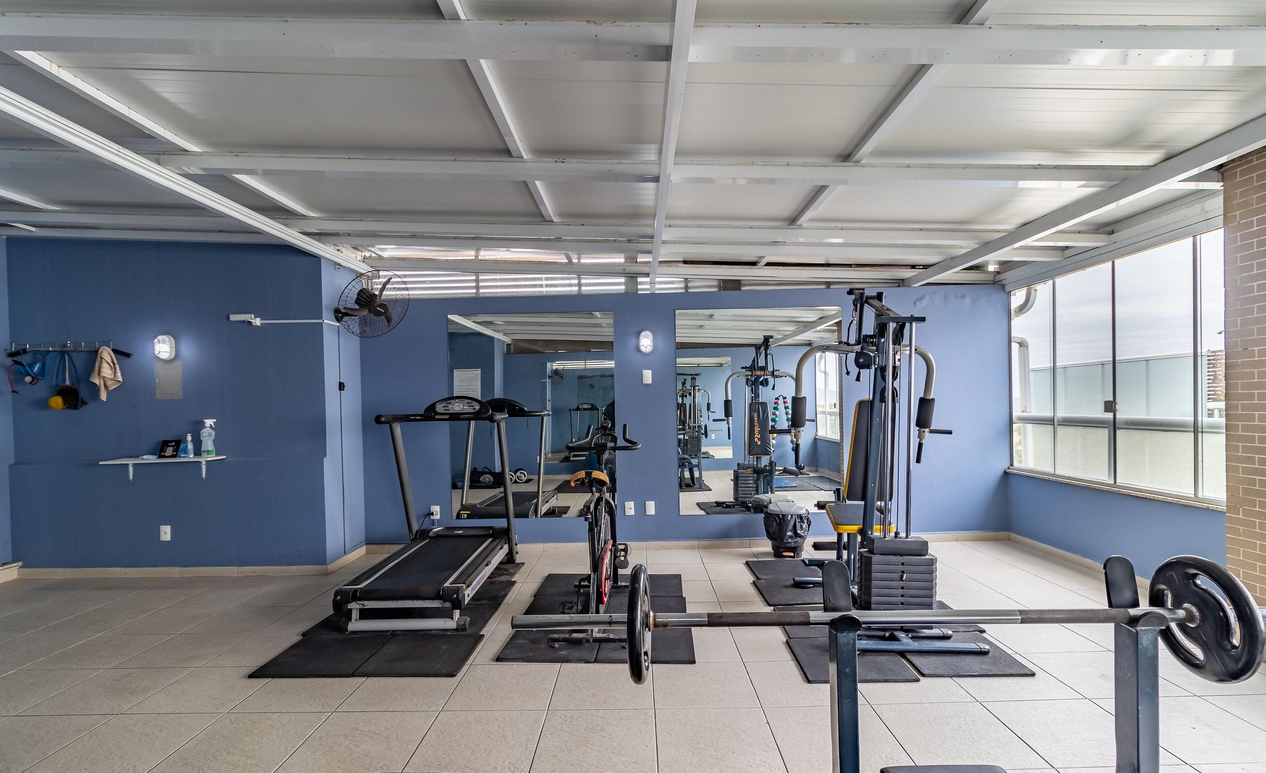 Academia com equipamentos de ginástica, esteira e espelho.
