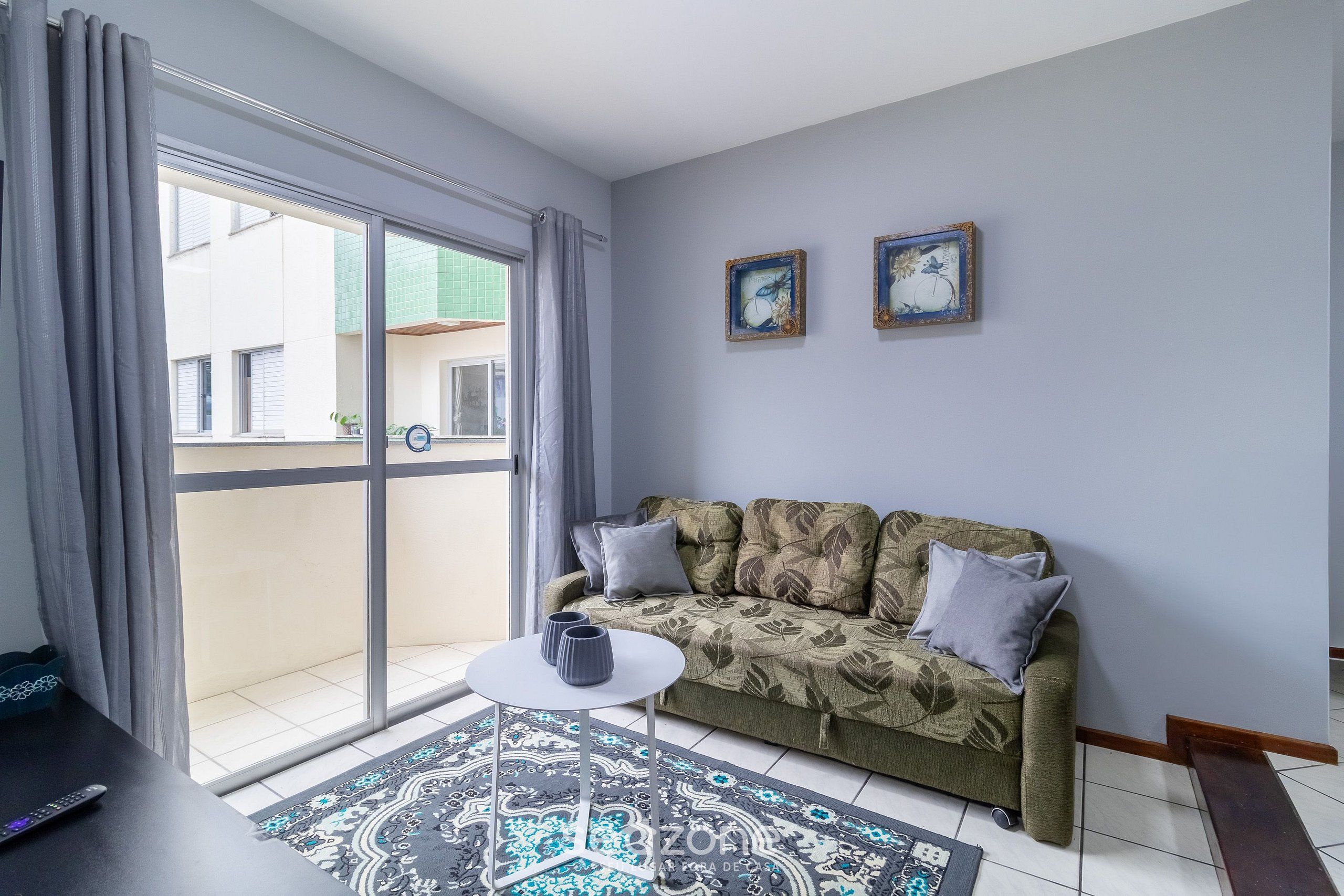 Sala de estar com sofá, mesinha, tapete estampado e porta de vidro deslizante para área externa.