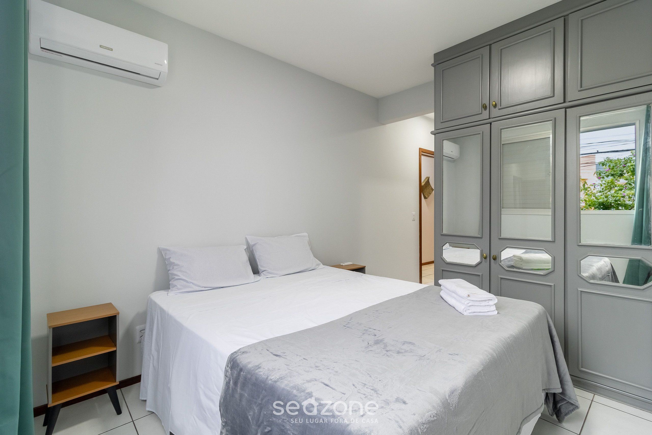 Quarto com cama, guarda-roupa, mesa de cabeceira e ar condicionado.