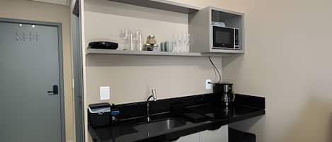 Uma cozinha compacta com bancada preta, micro-ondas e cafeteira.
