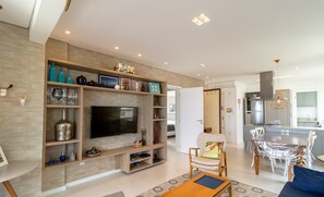 Uma sala de estar moderna com televisão de tela plana, estantes de madeira e um espaço de refeições com mesa e cadeiras.