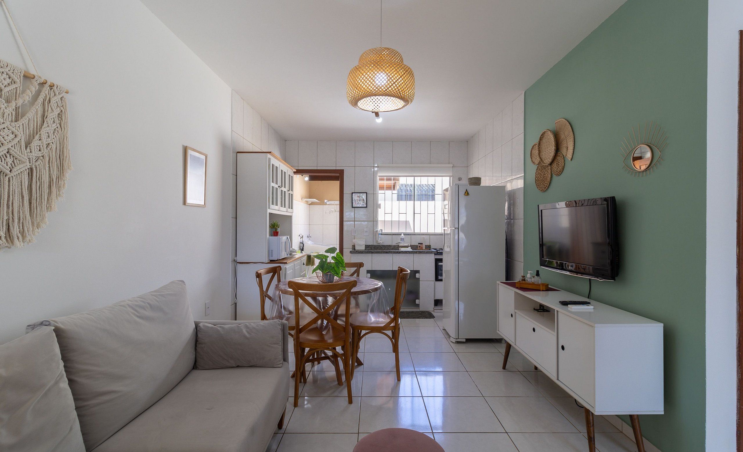 Uma sala de estar moderna com sofá, mesa de jantar, cadeiras, televisão e cozinha ao fundo.