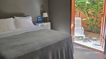 Quarto com cama, mesa de cabeceira, abajur e vista para um jardim através de uma porta de correr.