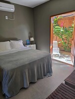 Quarto com cama, mesa de cabeceira, abajur e vista para um jardim através de uma porta de correr.