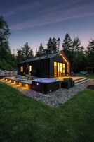 Uma cabana moderna com hidromassagem, deck e área de estar externa, rodeada por uma paisagem natural.