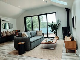 Uma sala de estar moderna com um sofá cinzento, uma mesa de centro de madeira e uma grande janela com vista para um lago.