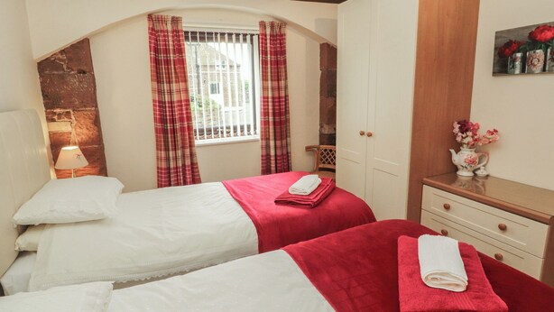 Quarto de hotel com duas camas, uma cômoda de madeira, um espelho, uma janela com cortinas e um quadro na parede.