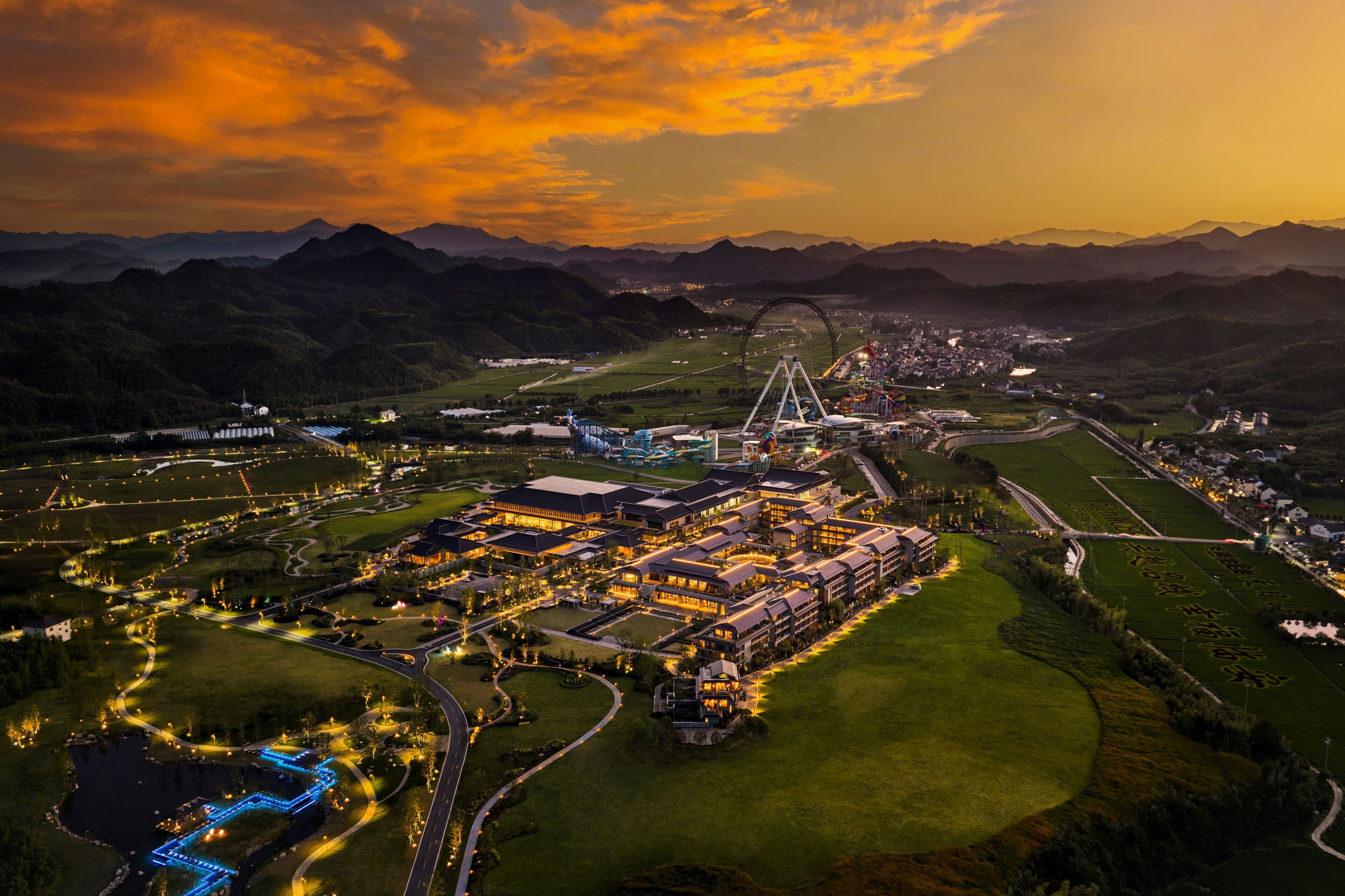 Vista aérea de um resort com vários edifícios, um grande parque de diversões e montanhas ao fundo.
