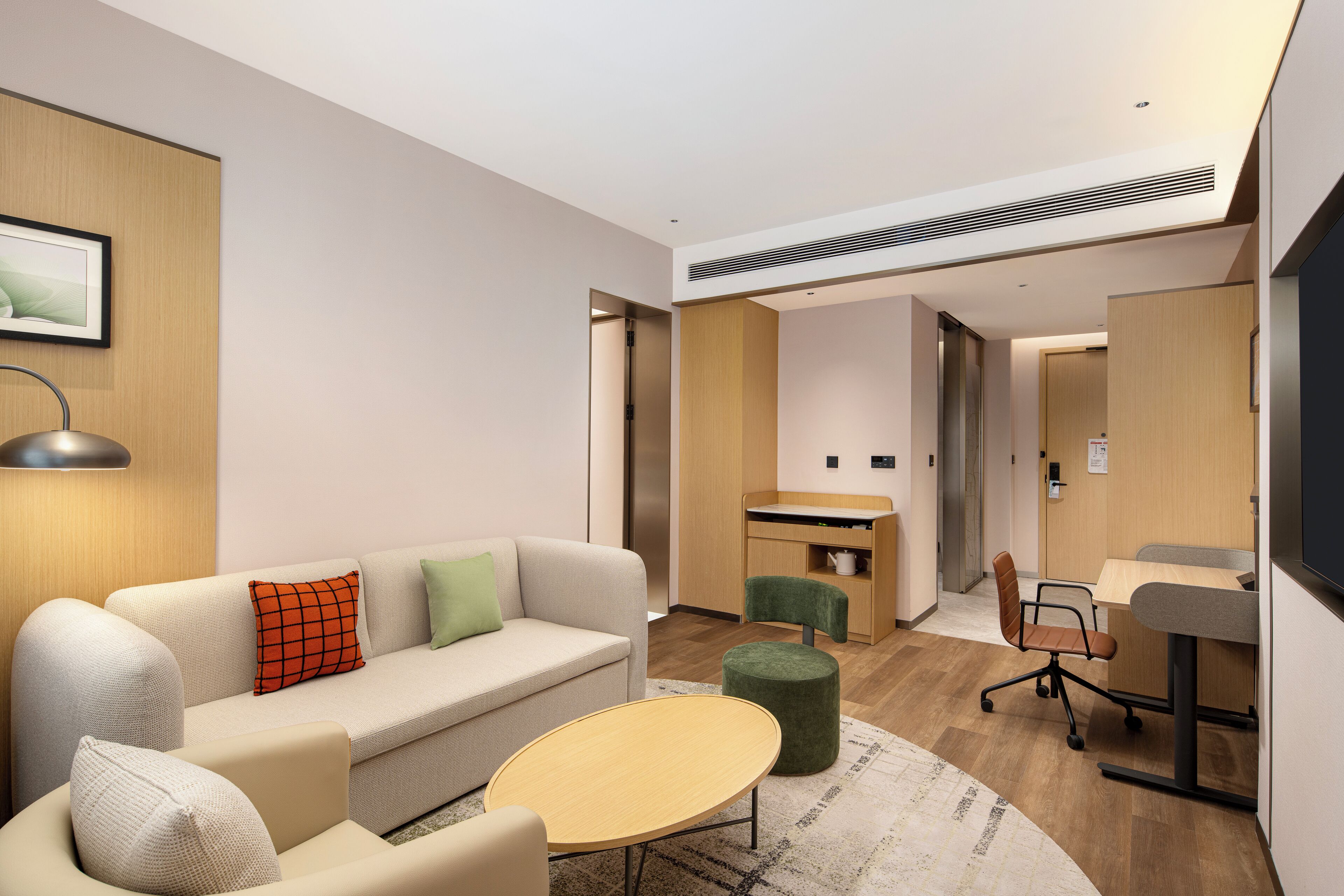 Quarto de hotel moderno com sofá, uma mesinha redonda, escrivaninha com cadeira e espaço para cozinha.