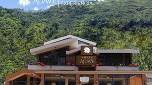 Um hotel moderno com uma placa indicando "HOTEL AGAVE" e o slogan "toda una experiencia". O edifício possui grandes janelas de vidro e um telhado plano.