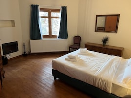 Quarto com cama, penteadeira, cadeira, radiador, janela com cortinas e espelho na parede.