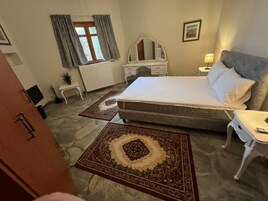 Quarto com cama grande, cómoda, mesa de cabeceira, luminária e janela com cortinas.
