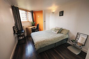 Quarto pequeno com cama, escrivaninha e cadeira.