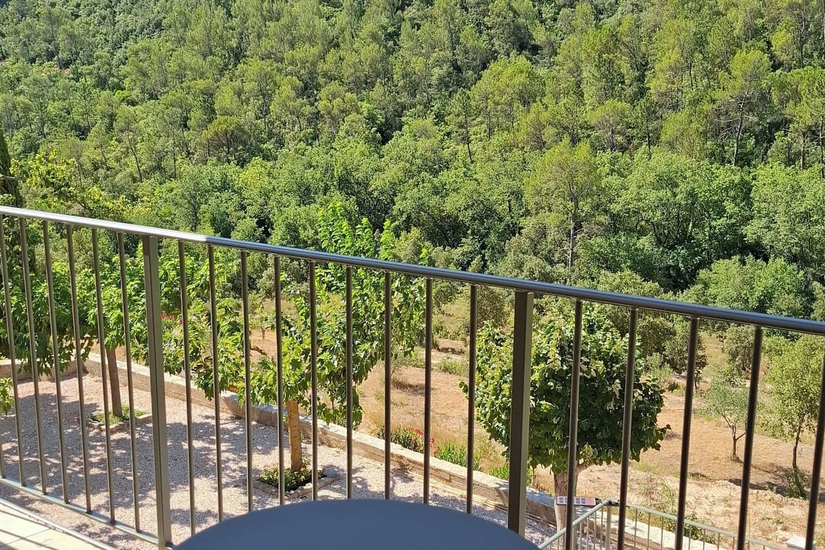 Varanda com mesa e cadeiras redondas, com vista para uma encosta arborizada.