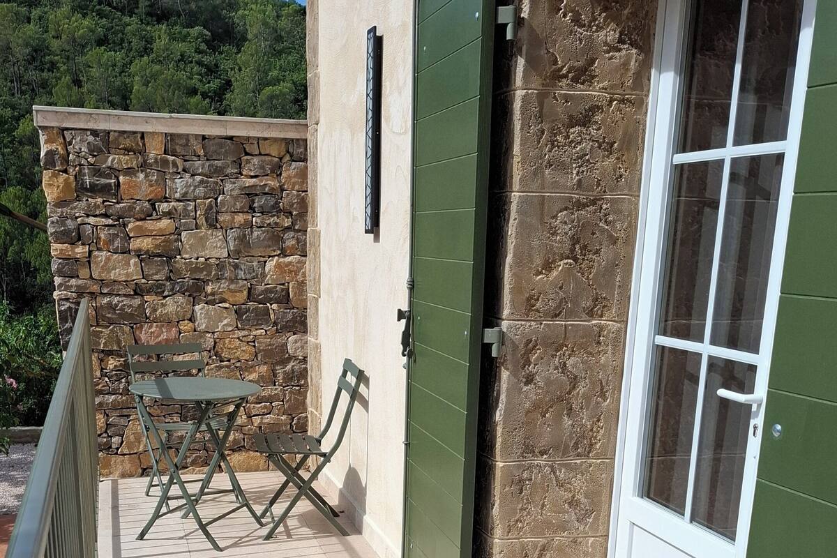 Uma varanda com parede de pedra, uma porta verde e uma mesa com cadeiras.