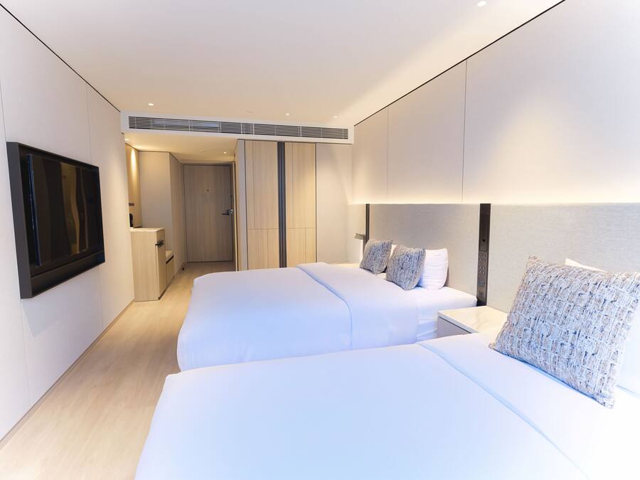 Quarto de hotel moderno com duas camas, TV fixada na parede e um closet espaçoso.