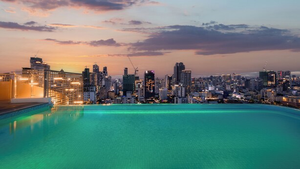 Silhueta urbana ao entardecer, com uma piscina em primeiro plano.