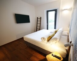 Quarto com cama, televisão na parede, janela com vista e piso de madeira.