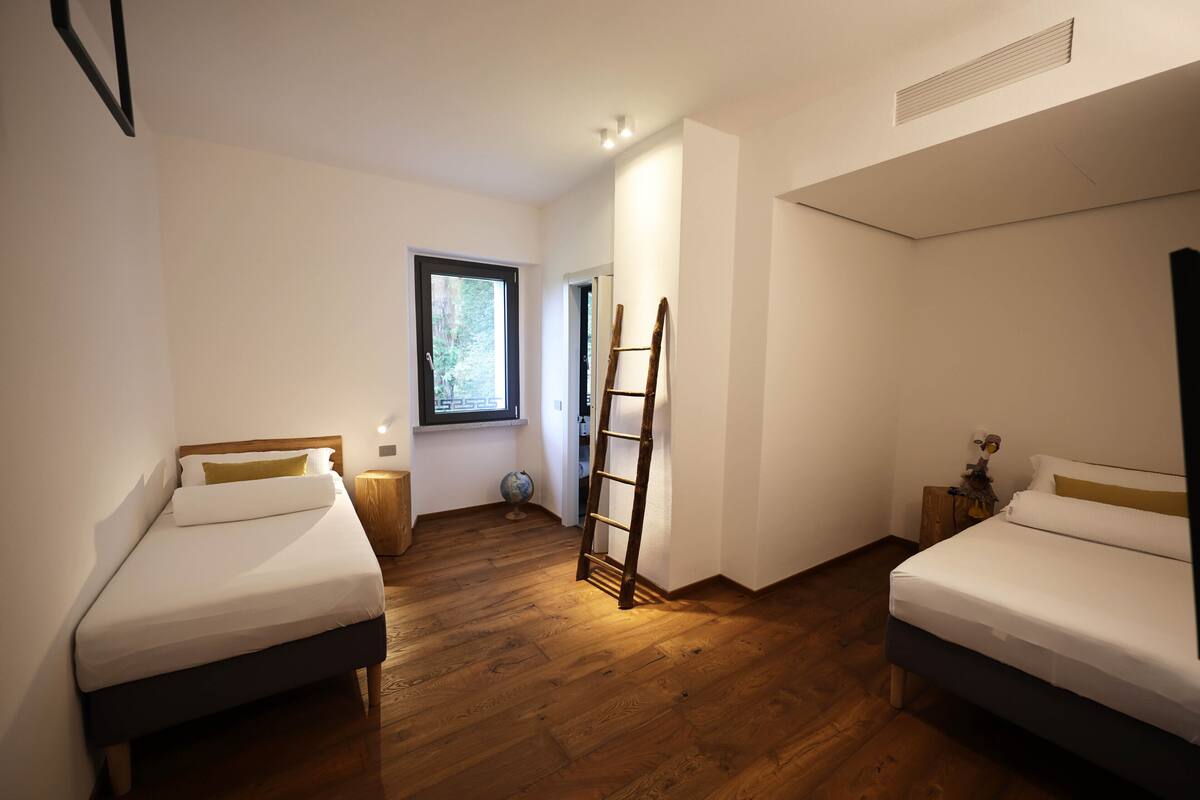 Quarto com duas camas, piso de madeira, escada, globo e janela com luz natural.