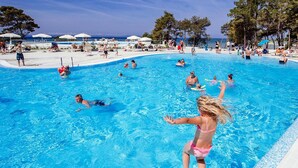 Piscina com pessoas aproveitando a água, cercada por espreguiçadeiras e guarda-sóis.