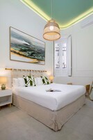 Quarto bem arrumado com uma cama grande, luminária pendente, um quadro e uma janela com grades.