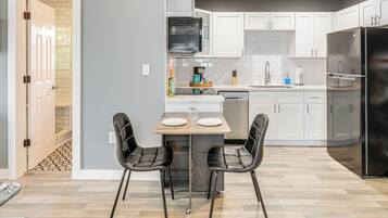 Uma cozinha moderna com armários brancos, uma geladeira preta e um espaço de refeições com duas cadeiras e uma mesa.
