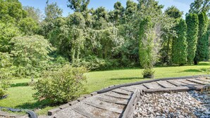 Um jardim com um caminho de cascalho e uma estrutura de madeira curva, rodeado por vegetação exuberante e árvores.