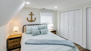Quarto com cama, mesas de cabeceira, decoração pendurada na parede, janela com persianas e armário.