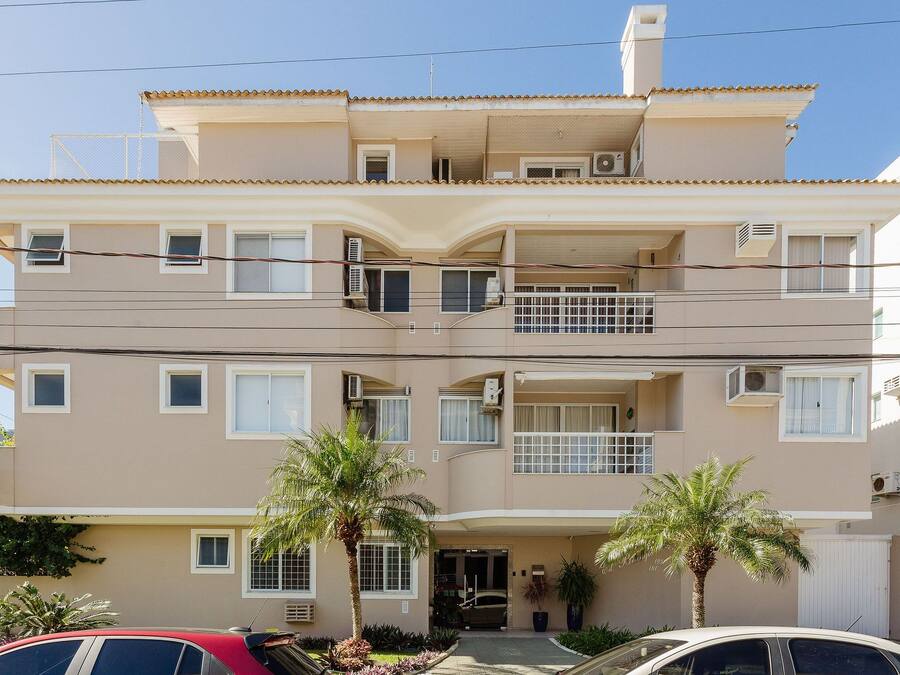 Um edifício residencial com várias andares, varandas, aparelhos de ar condicionado e entrada com portão.