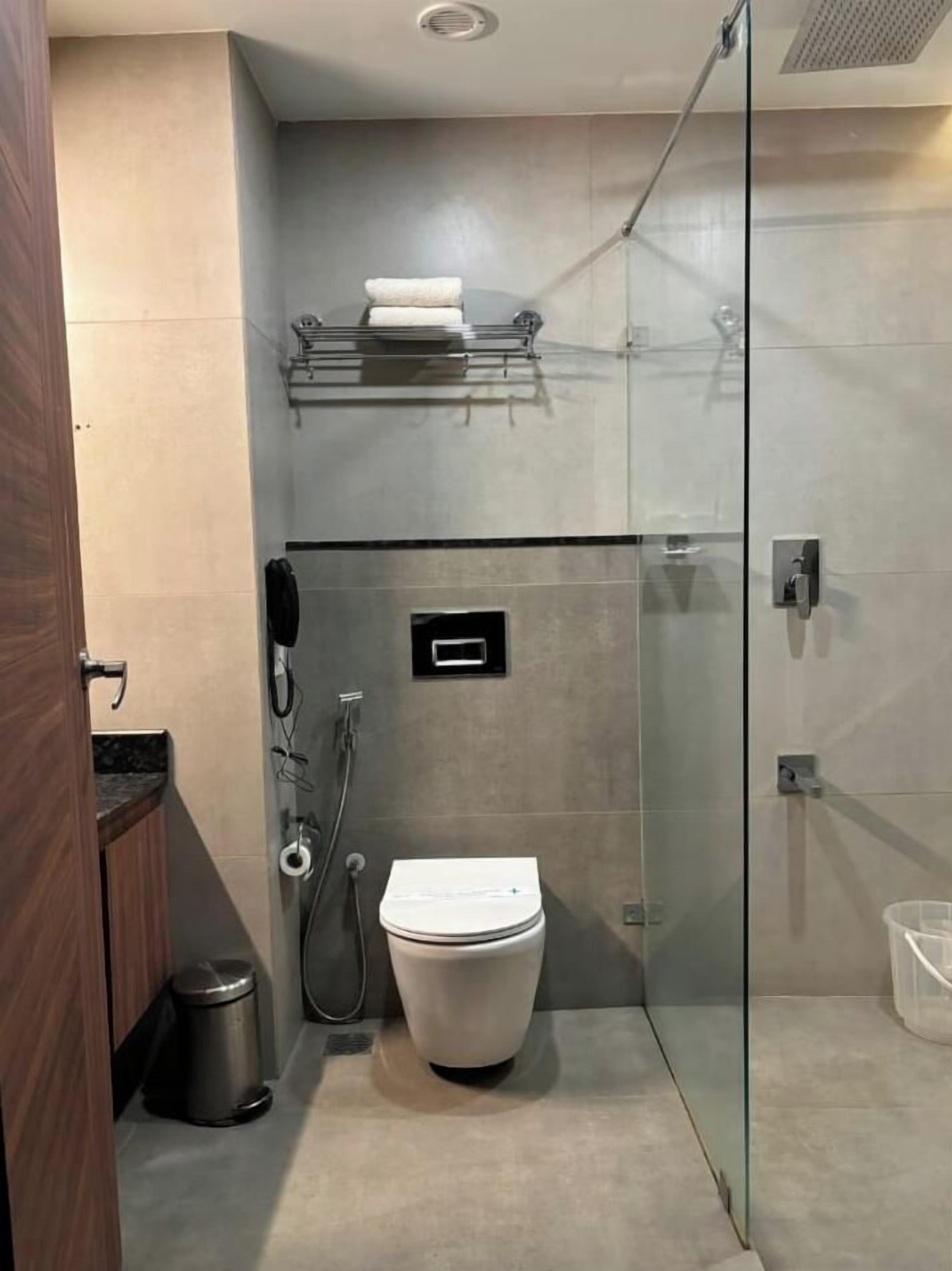 Um banheiro moderno com box de vidro, vaso sanitário, lixeira e porta-toalhas.