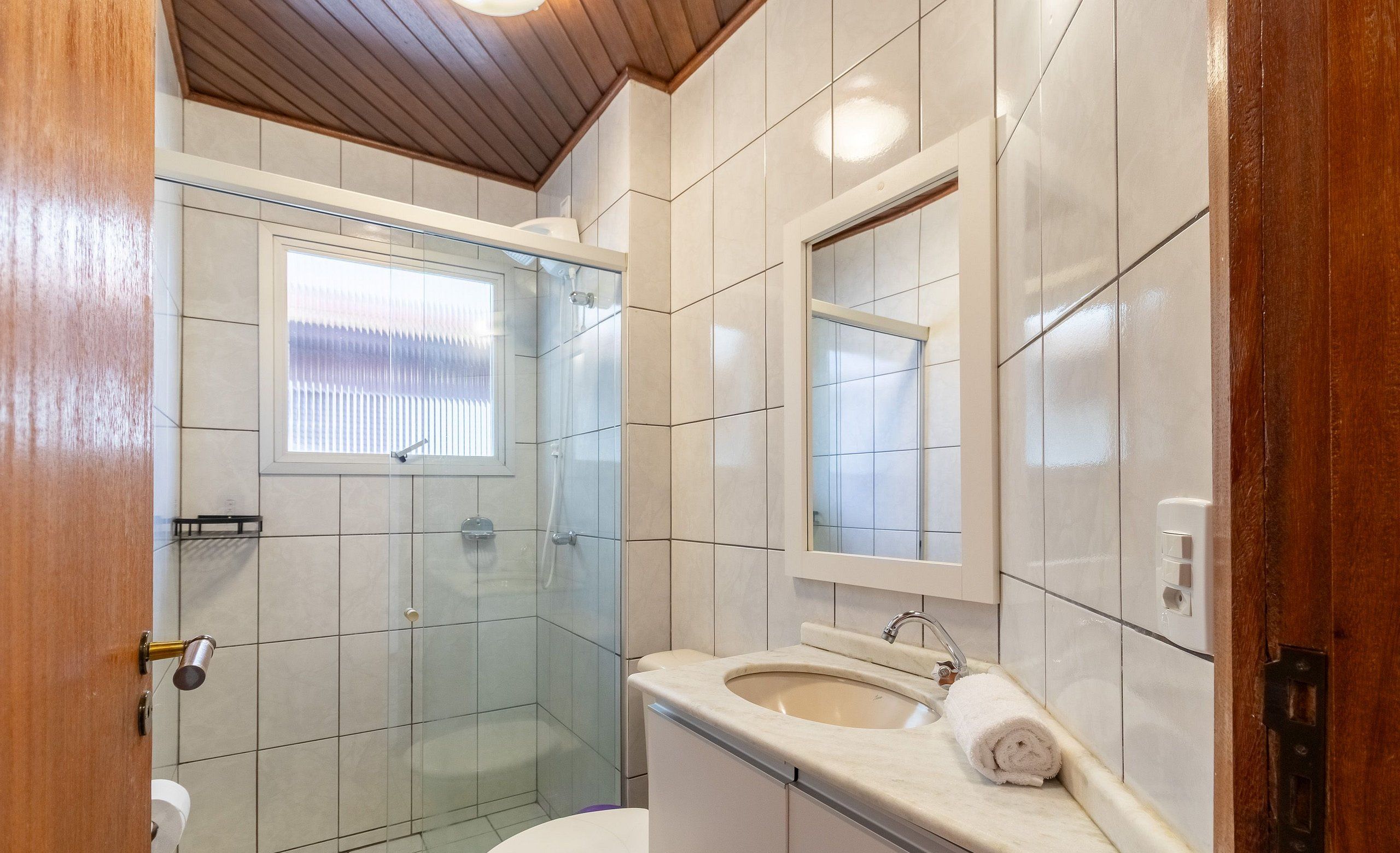Uma casa de banho com cabine de duche em vidro, sanita, lavatório com espelho e toalha no balcão.