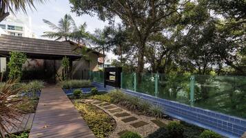 Uma trilha leva a um edifício com entrada coberta, cercado por vegetação exuberante e uma parede de azulejos azuis.