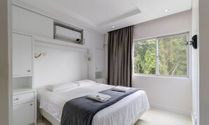 Quarto moderno com cama grande, espaço de armazenamento embutido, janela com vista para árvores e luminária de teto.
