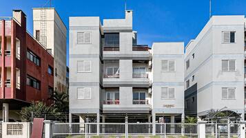 Edifício residencial com vários andares, varandas, portão fechado e céu claro.
