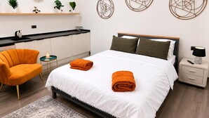 Quarto moderno com cama, mesa de cabeceira, cadeira e arte decorativa na parede.