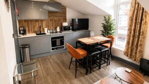 Cozinha moderna com armários cinza, micro-ondas e televisão. Possui área de jantar com mesa de madeira e cadeiras laranja.