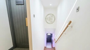 Um corredor com corrimão de madeira, um detalhe decorativo na parede com padrão geométrico e uma porta com a inscrição 