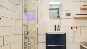 Um banheiro com paredes revestidas de azulejos brancos, pia preta, espelho e piso com ladrilhos estampados.