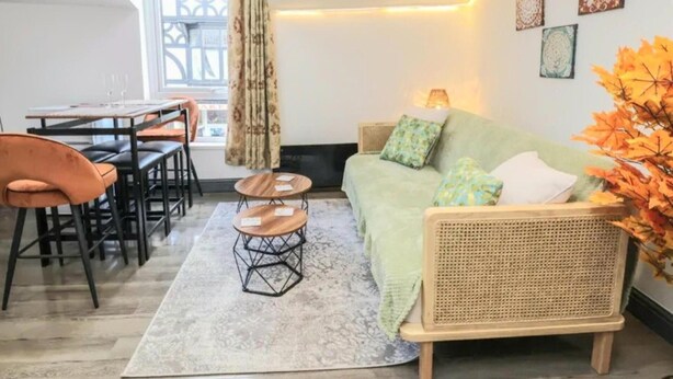 Uma sala de estar moderna com um sofá, uma mesa de jantar com cadeiras, uma mesa de centro redonda e uma janela com cortinas.