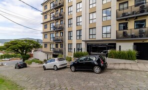 Um edifício residencial com várias andares, varandas, um caminho de entrada pavimentado e carros estacionados.
